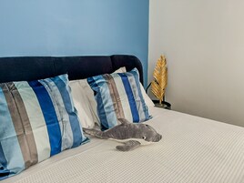 Uma cama com almofadas listradas e um brinquedo de tubarão de pelúcia cinza sobre um colchão branco texturizado.