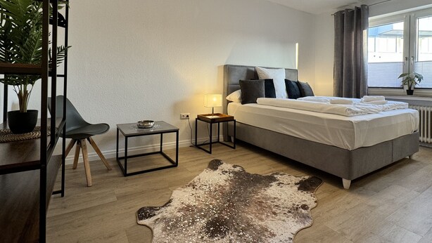 Quarto moderno com uma cama grande, uma mesinha de cabeceira, uma cadeira, um vaso com planta e um tapete de couro de vaca exclusivo.
