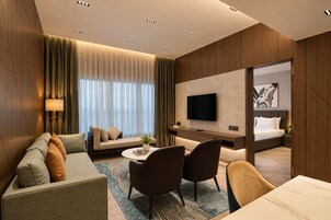 Quarto de hotel com sofá, cadeiras, escrivaninha, televisão e cama.