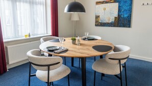 Uma mesa de jantar redonda com quatro cadeiras, uma luminária pendente, um quadro na parede e uma janela com cortinas.