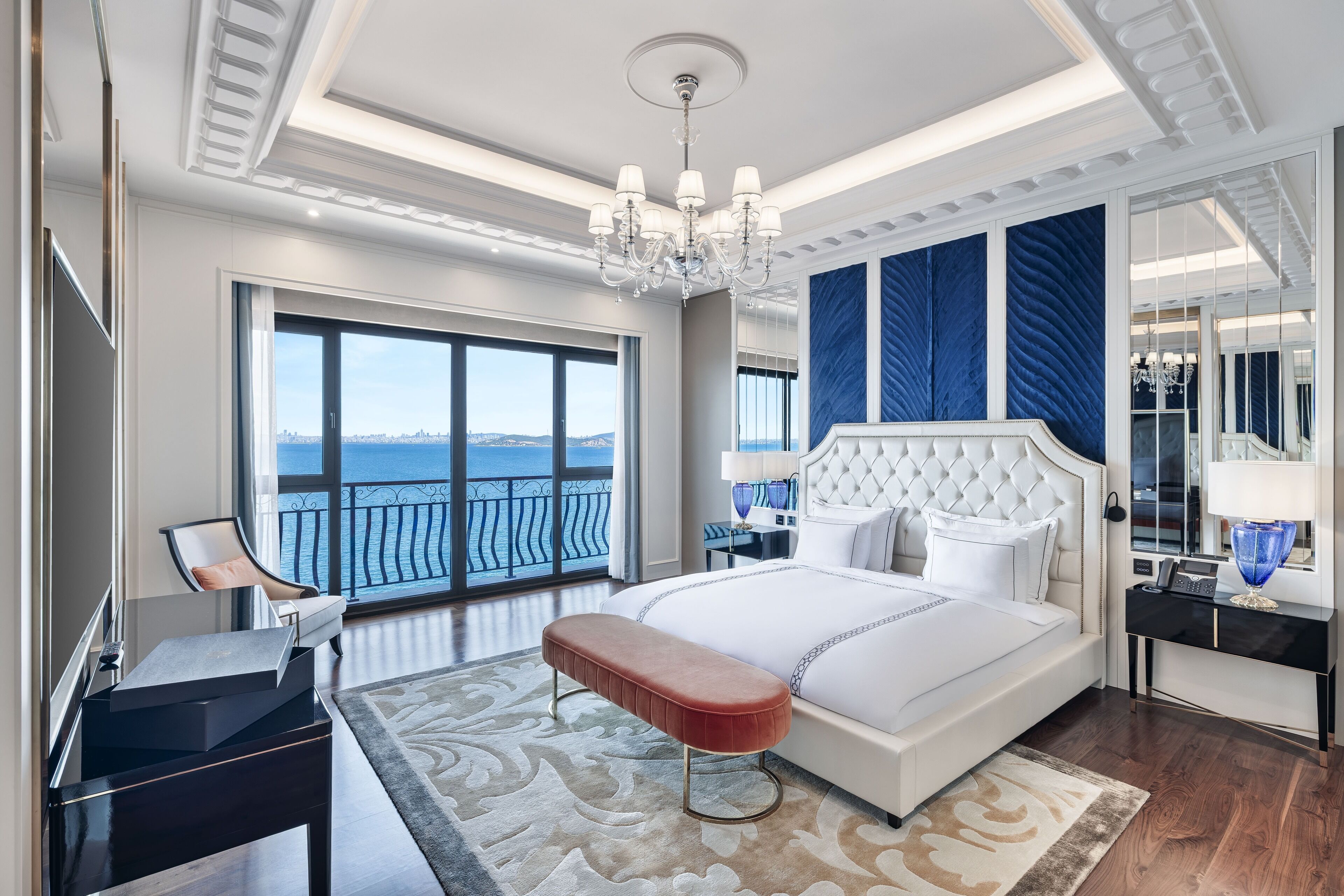 Quarto de hotel moderno com uma cama grande, um banco, uma escrivaninha e vista para o mar.