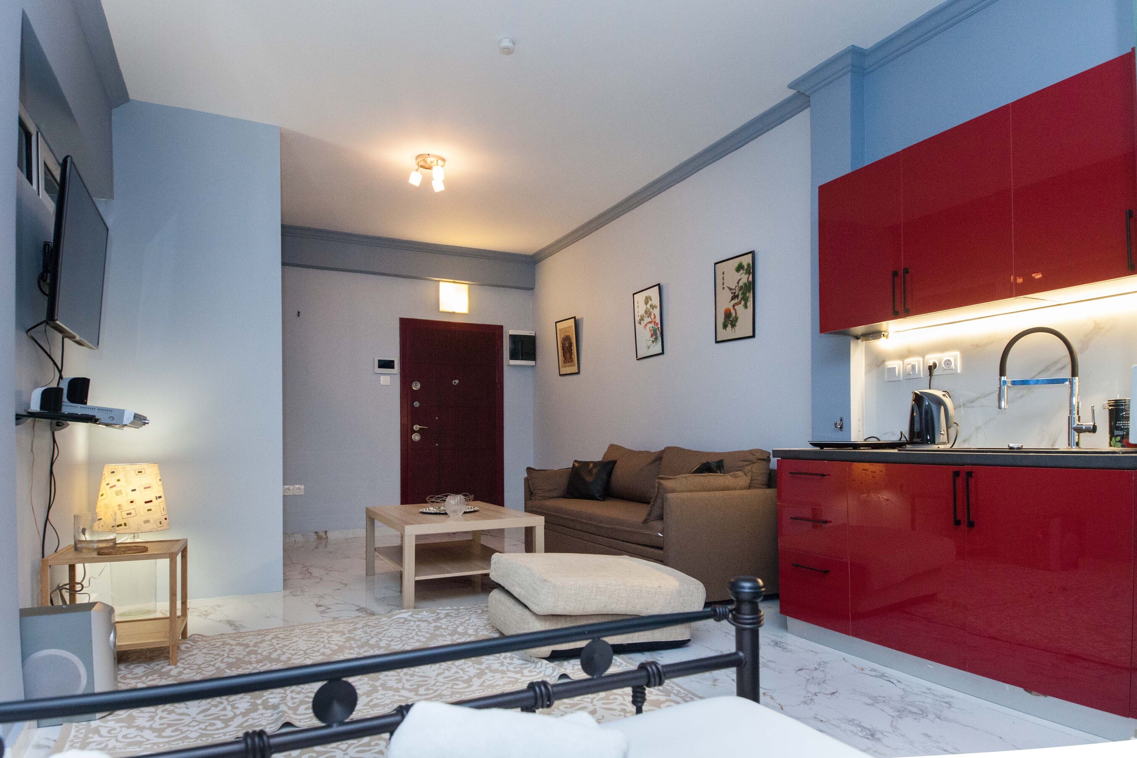 Um espaço de estar compacto com cama, sofá, uma mesa pequena, televisão e uma cozinheira com armários vermelhos.