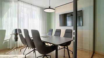 Uma sala de conferências com uma mesa comprida, seis cadeiras e um janelão com cortinas leves.