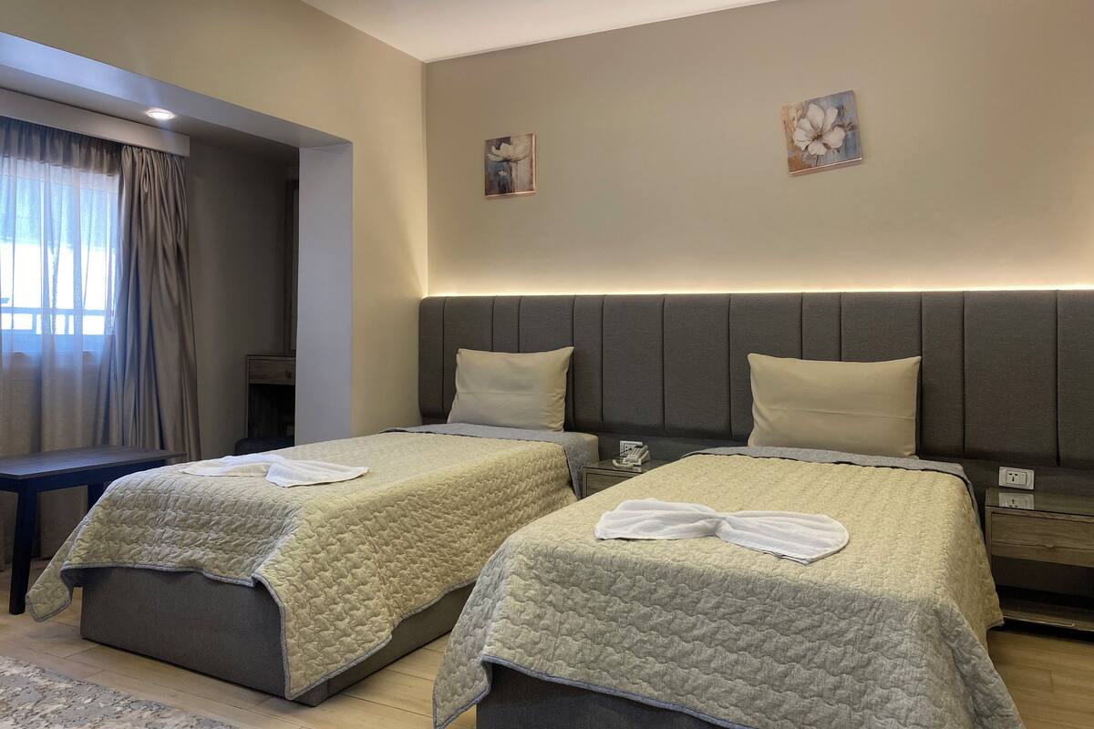 Quarto de hotel com duas camas, uma escrivaninha e uma mesa de cabeceira.
