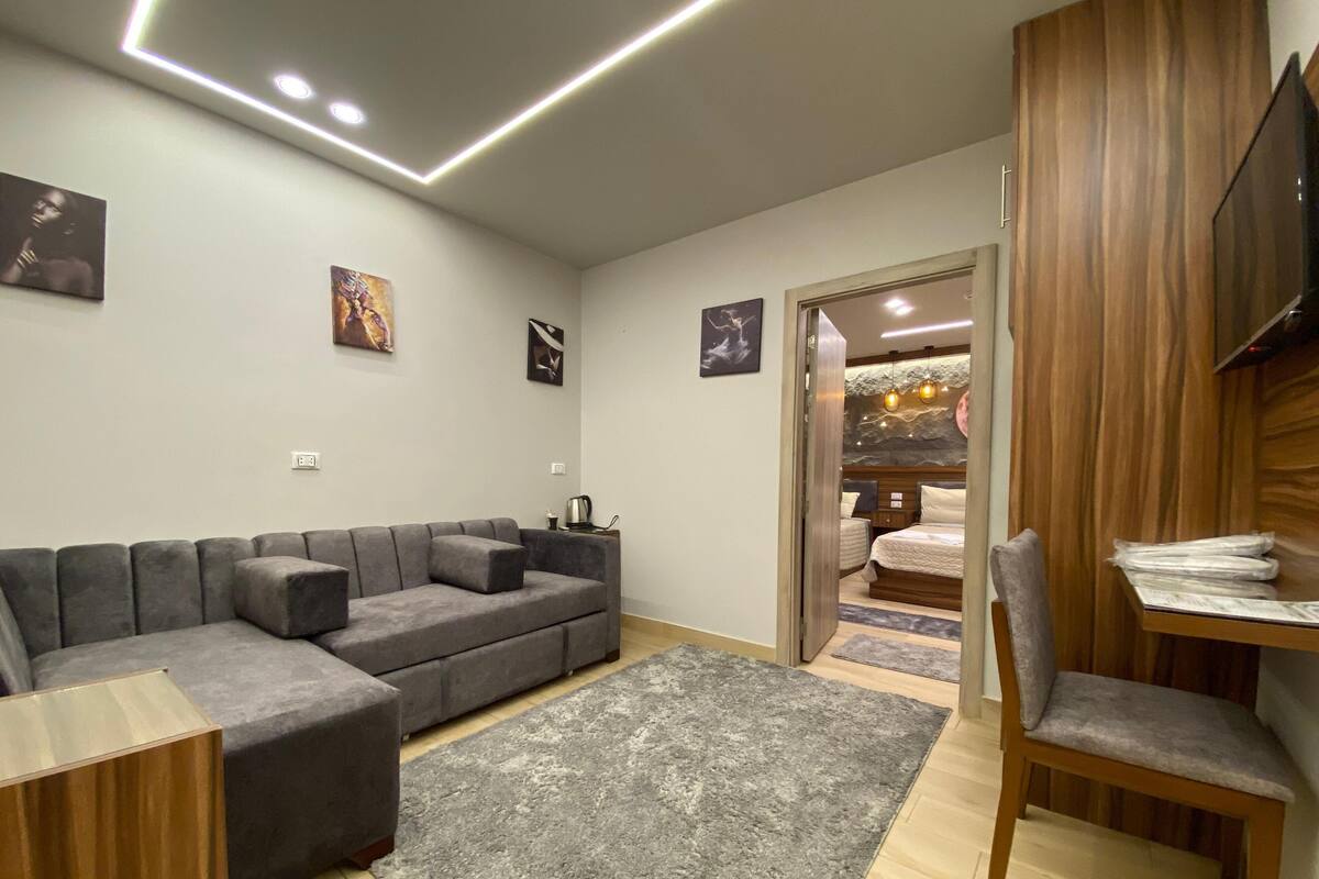 Uma sala de estar moderna com um sofá modular cinza, uma mesa lateral de madeira, um tapete cinza e uma cadeira de madeira.
