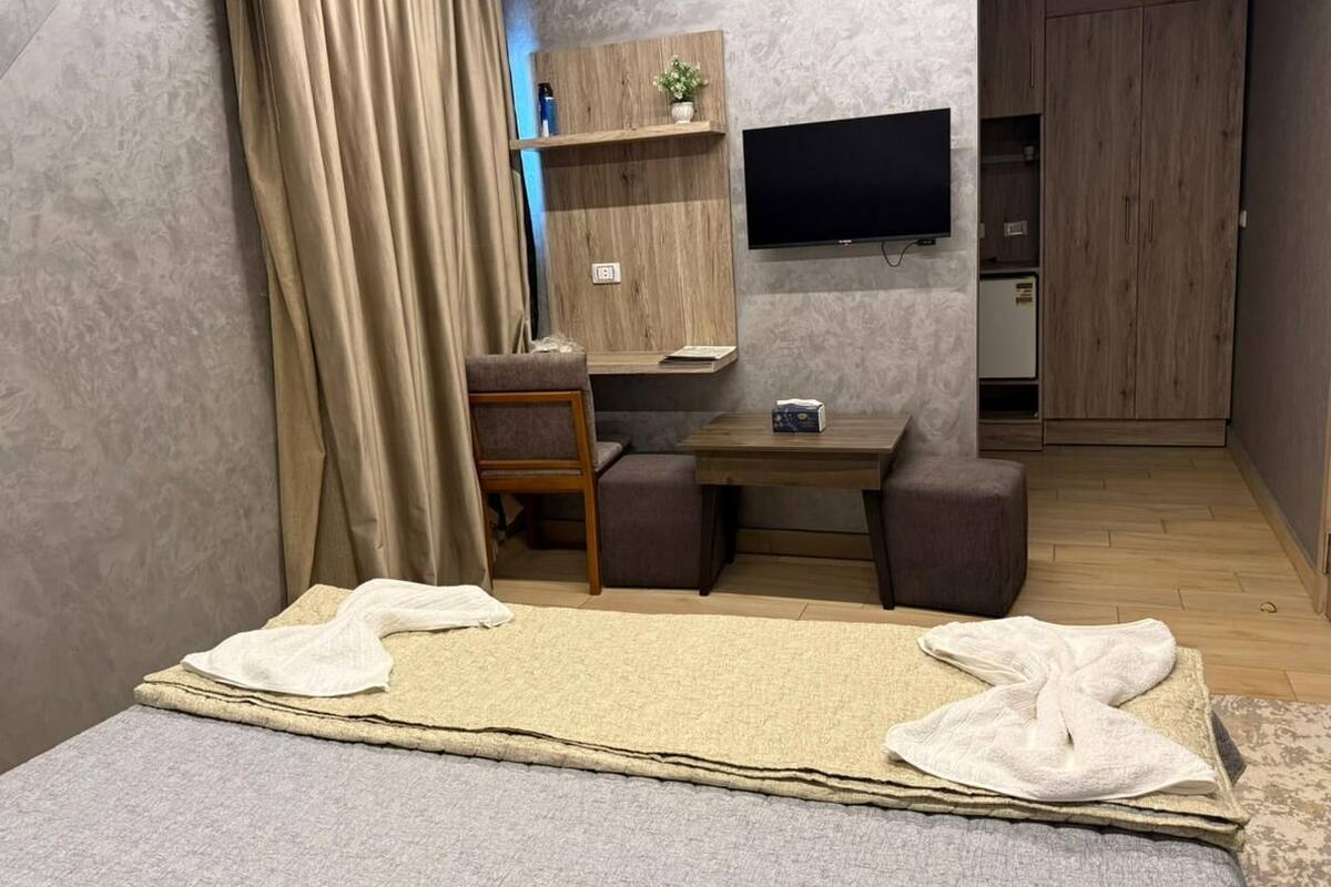 Quarto de hotel com cama, escrivaninha, cadeira, televisão e guarda-roupa.