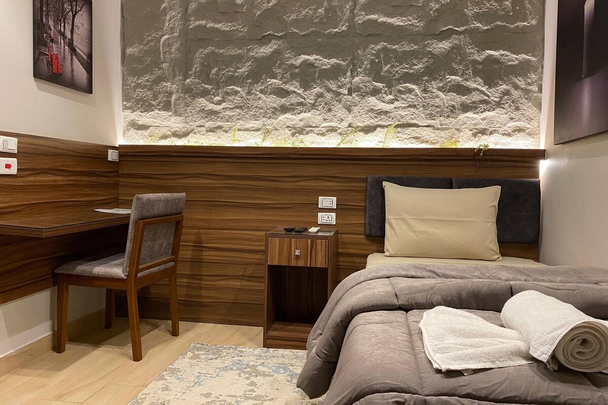 Quarto de hotel com uma cama, uma escrivaninha e uma cadeira. Um grande mural na parede retrata uma paisagem rochosa.