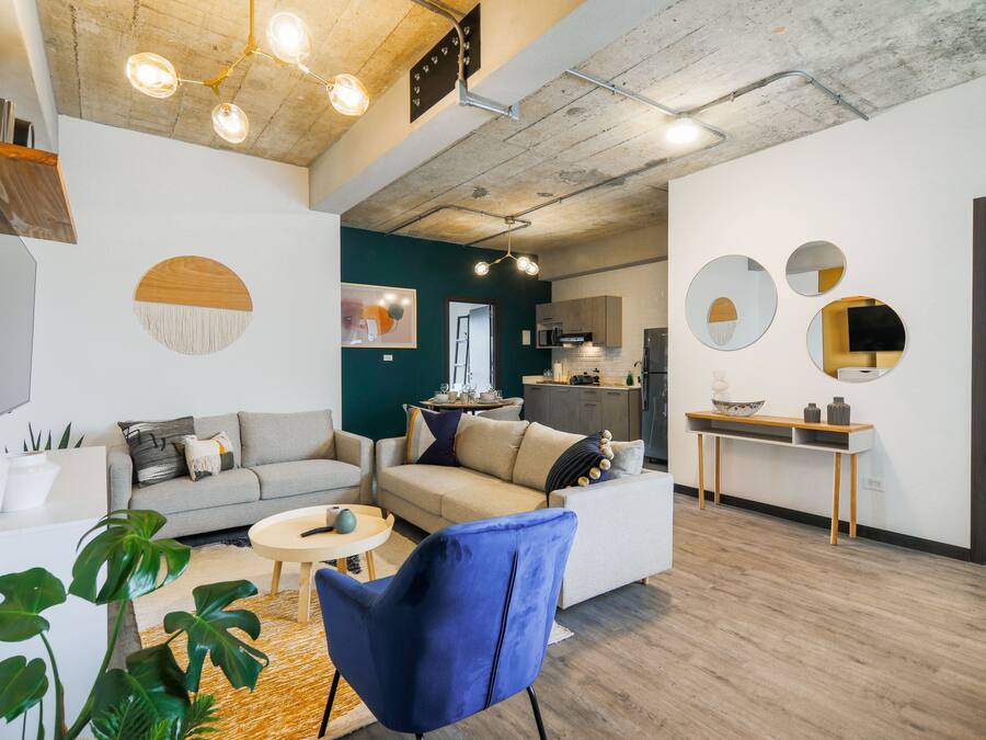Uma sala moderna com sofá, poltrona e mesa de centro, cozinha com armários e eletrodomésticos, e mesa de jantar com cadeiras.