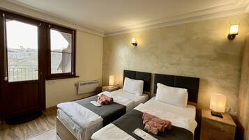 Quarto de hotel com duas camas, uma janela, um radiador e uma mesa de cabeceira com abajur.