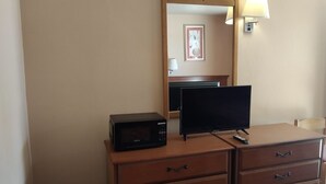Quarto de hotel com cômoda de madeira, televisão de tela plana, micro-ondas, luminária e quadro na parede.