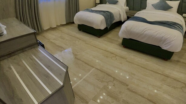 Quarto de hotel moderno com duas camas, uma escrivaninha e uma janela grande com cortinas.