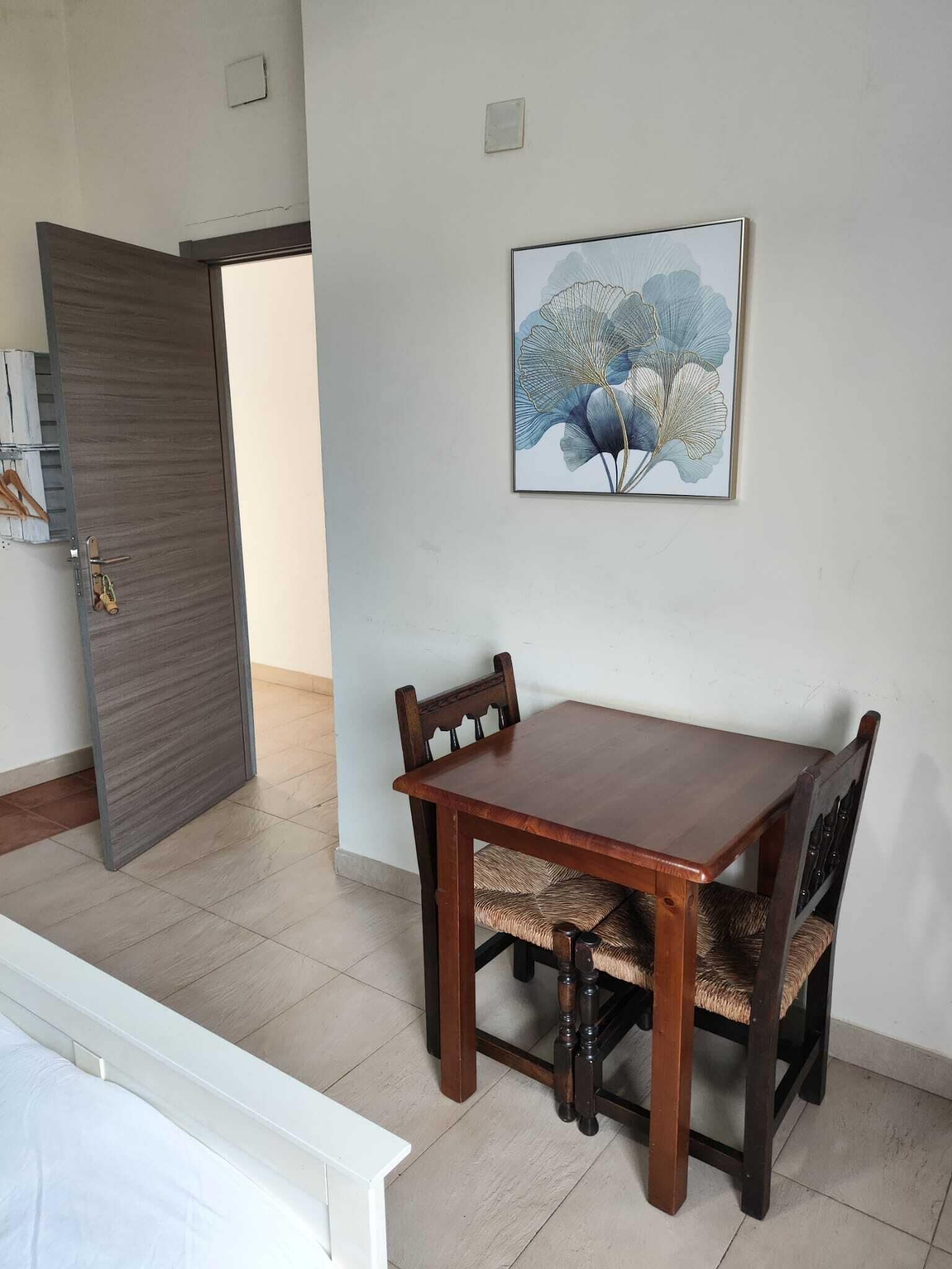 Uma sala de jantar com mesa e cadeiras de madeira, um quadro na parede e uma porta entreaberta.