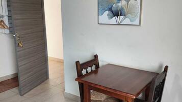 Uma sala de jantar com mesa e cadeiras de madeira, um quadro na parede e uma porta entreaberta.