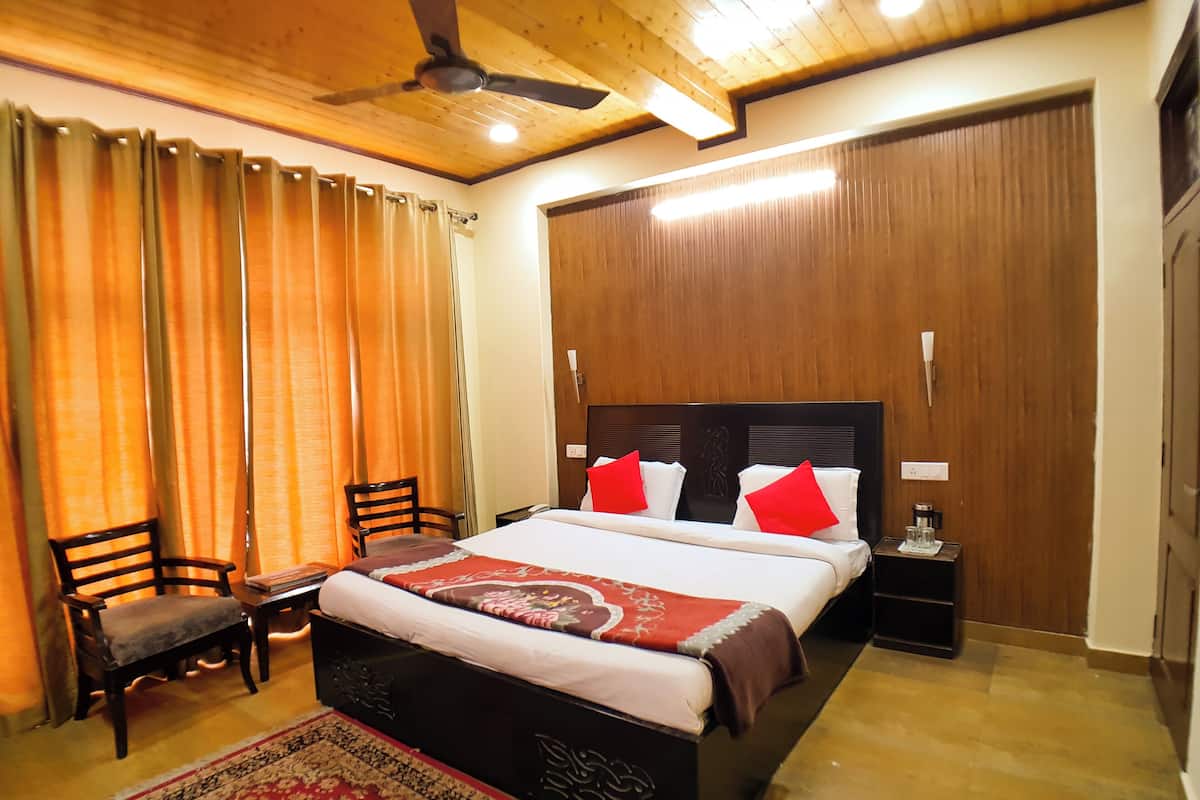 Um quarto com cama, duas cadeiras, mesa de cabeceira, ventoinha de madeira no teto e um guarda-roupa grande.