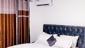 Quarto com uma cama grande, cabeceira estofada escura, roupa de cama branca e ar-condicionado fixado na parede.