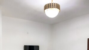 Quarto com uma cama, um sofá, uma mesa pequena, televisão fixada na parede e um candelabro.