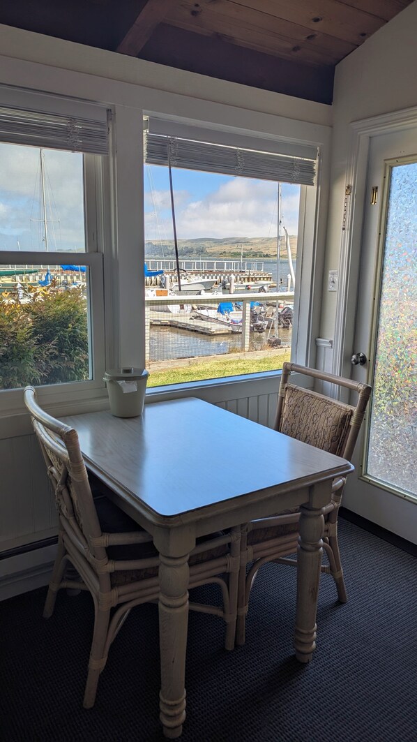 Uma área de refeições com mesa e cadeiras, uma janela com vista para um porto de iates e uma porta com vidro fosco.