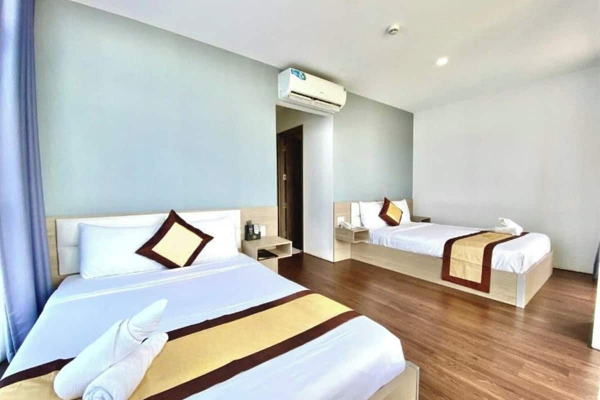 Quarto de hotel com duas camas, piso de madeira, ar condicionado montado no teto e uma porta que dá para outro cômodo.
