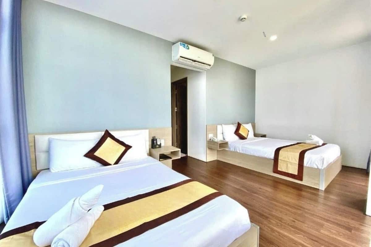Quarto de hotel com duas camas, piso de madeira, ar condicionado e uma porta que dá para outro quarto.