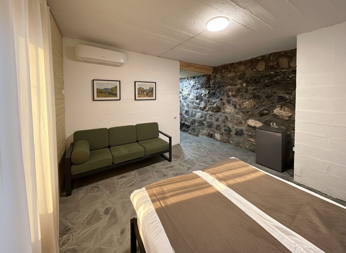 Um quarto com uma cama, um sofá verde, duas imagens emolduradas, uma parede de pedra e um aparelho de ar condicionado.