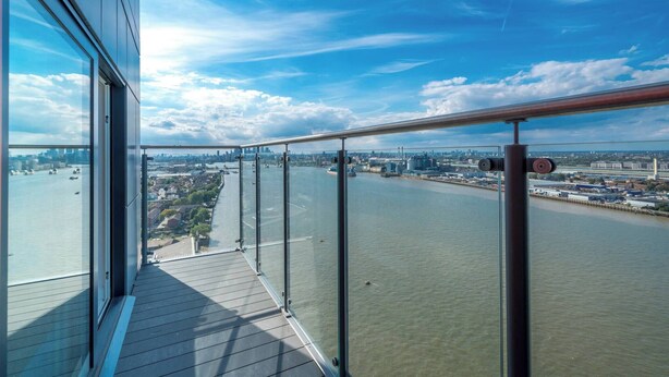 Um edifício alto com varanda de vidro, com vista para o rio e a paisagem urbana.