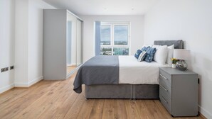 Quarto moderno com cama, mesa de cabeceira e uma grande janela com vista para a cidade.
