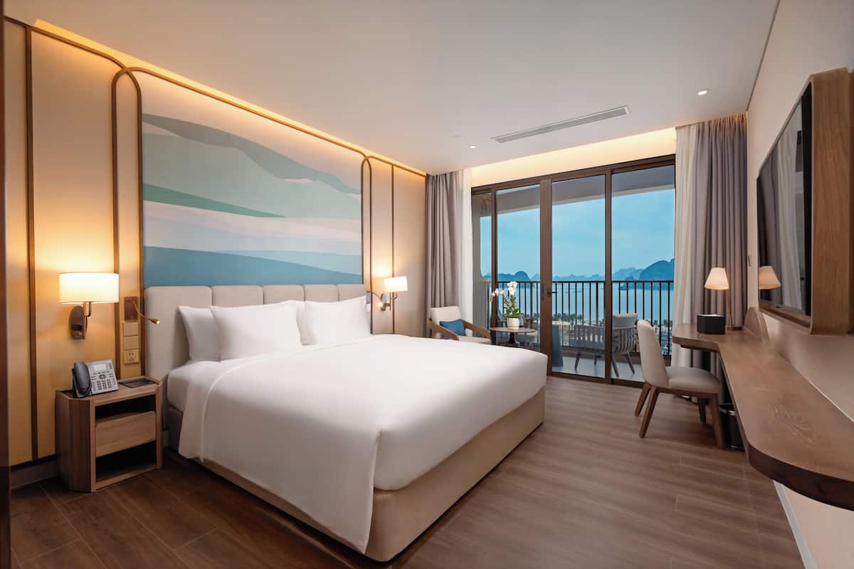 Quarto de hotel moderno com uma cama grande, abajures, uma mesa de trabalho e vista para a cidade.