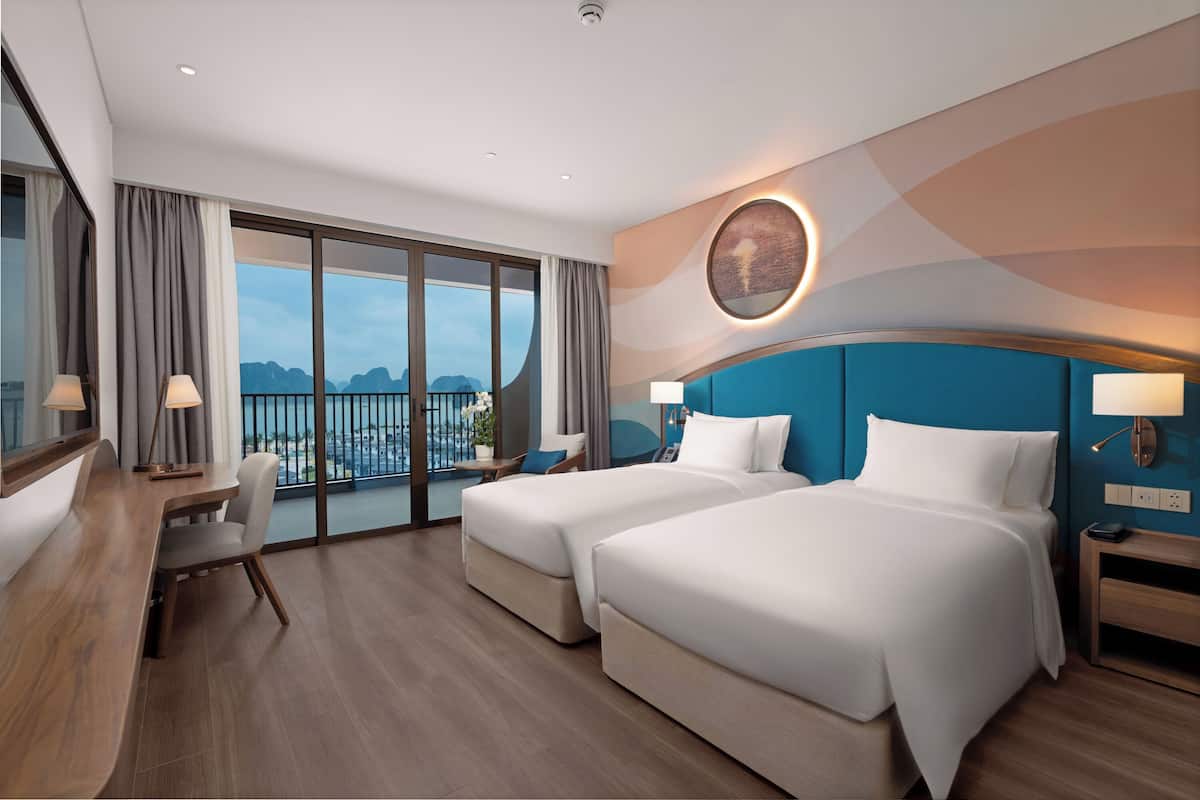 Quarto de hotel com duas camas, uma mesa e vista para as montanhas.