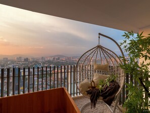 Quarto com cadeira suspensa, vista para a cidade e uma planta.