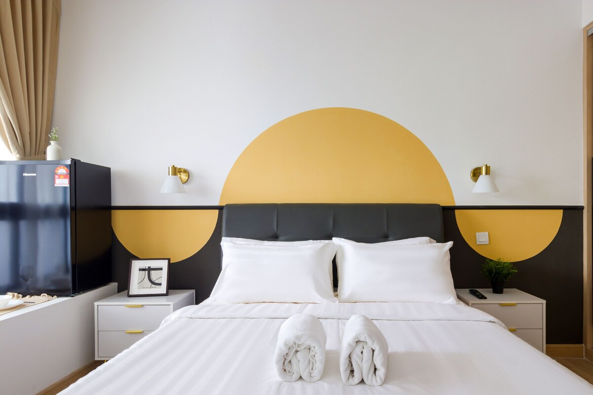 Quarto de hotel com cama, duas mesas de cabeceira, um criado-mudo, TV fixada na parede e guarda-roupa de madeira.