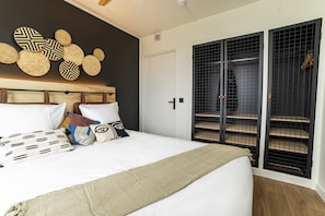 Quarto com cama, almofadas, cabeceira, parede com cestos de vime e um armário com porta de grade de metal.