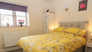 Um quarto com cama, janela florida, radiador e luminária fixada na parede.