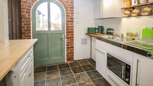 Uma cozinha com porta verde, armários brancos, forno embutido e uma prateleira com utensílios de cozinha.