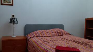 Quarto com cama, mesa de cabeceira, luminária, porta-retrato e lustre.