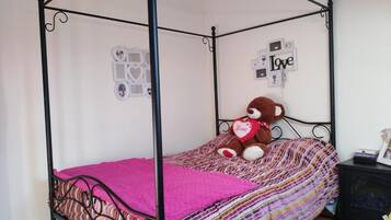 Uma cama de dossel com um cobertor rosa, um ursinho de pelúcia com um coração e decorações nas paredes.