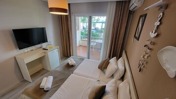 Quarto de hotel com cama, escrivaninha, televisão e varanda com cortinas.