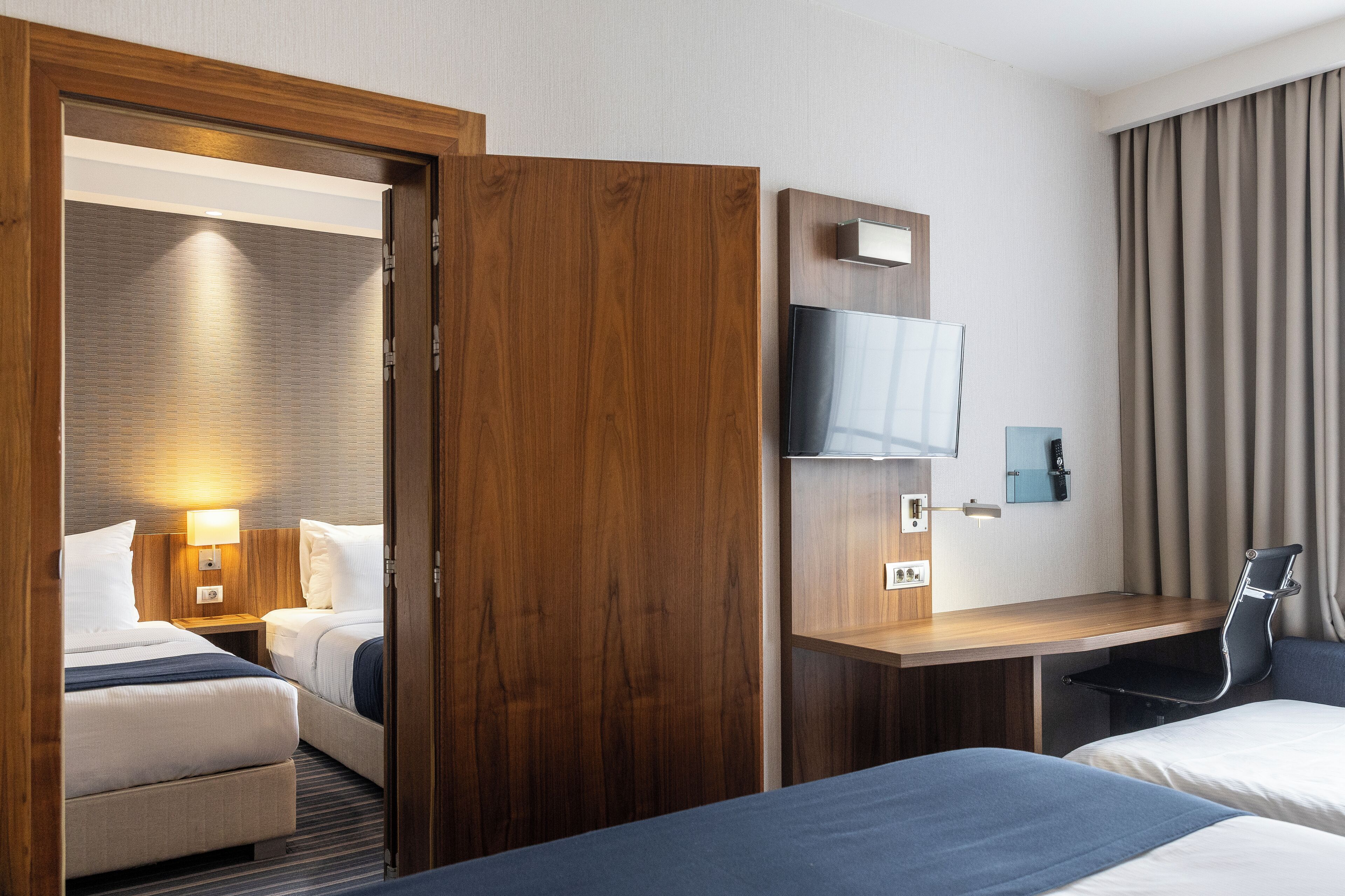 Quarto de hotel com duas camas, uma mesa, uma televisão e uma janela com cortinas.