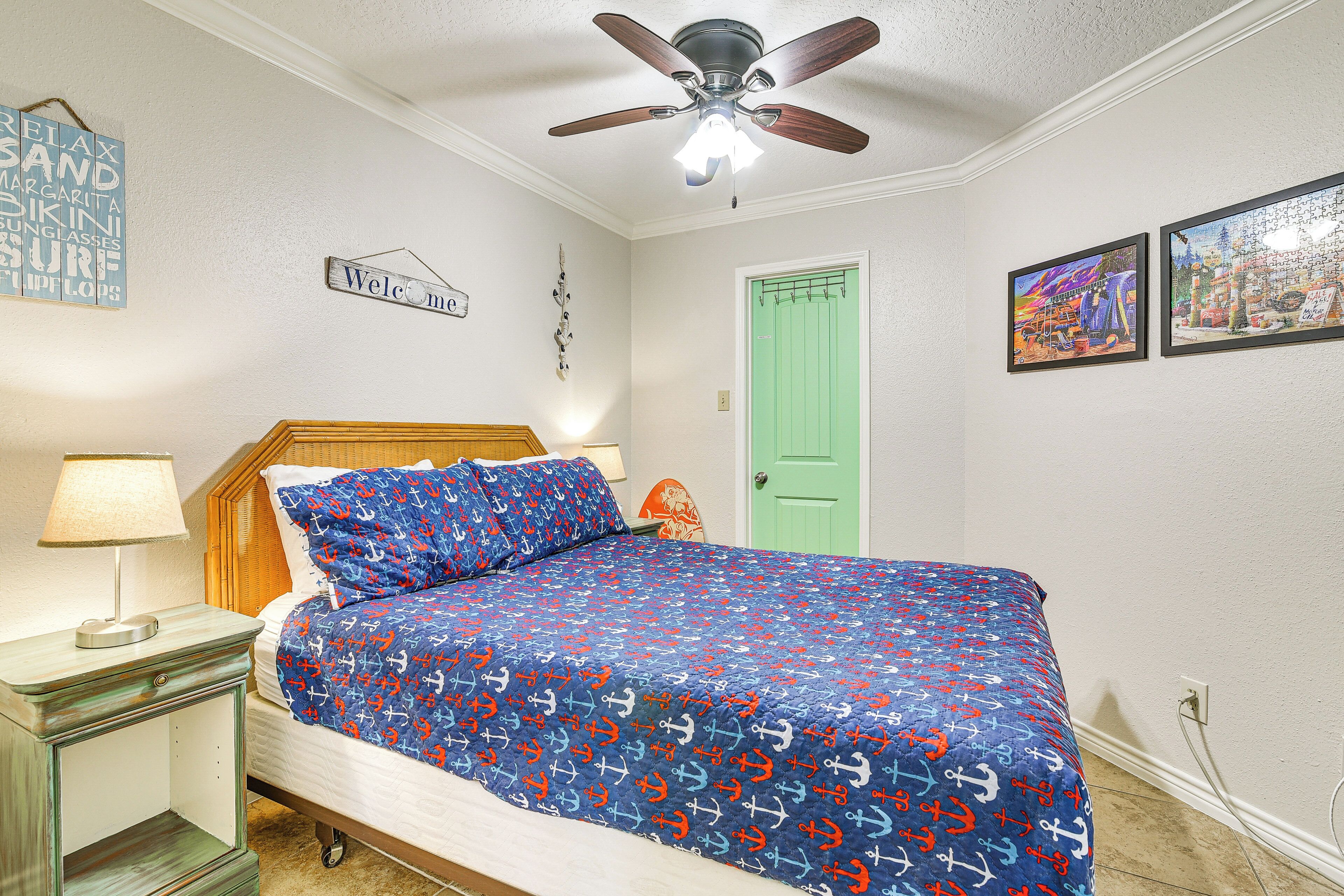Quarto com cama, mesa de cabeceira, ventilador de teto, porta verde e decorações nas paredes.
