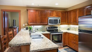 Cozinha com armários de madeira, bancadas de granito, eletrodomésticos de aço inoxidável e backsplash revestido com azulejos.
