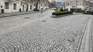 Uma praça de paralelepípedos com edifícios históricos, uma placa de indicação e um pedestre.