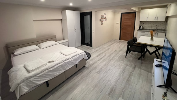 Quarto moderno com cama grande, escrivaninha e cozinha compacta.
