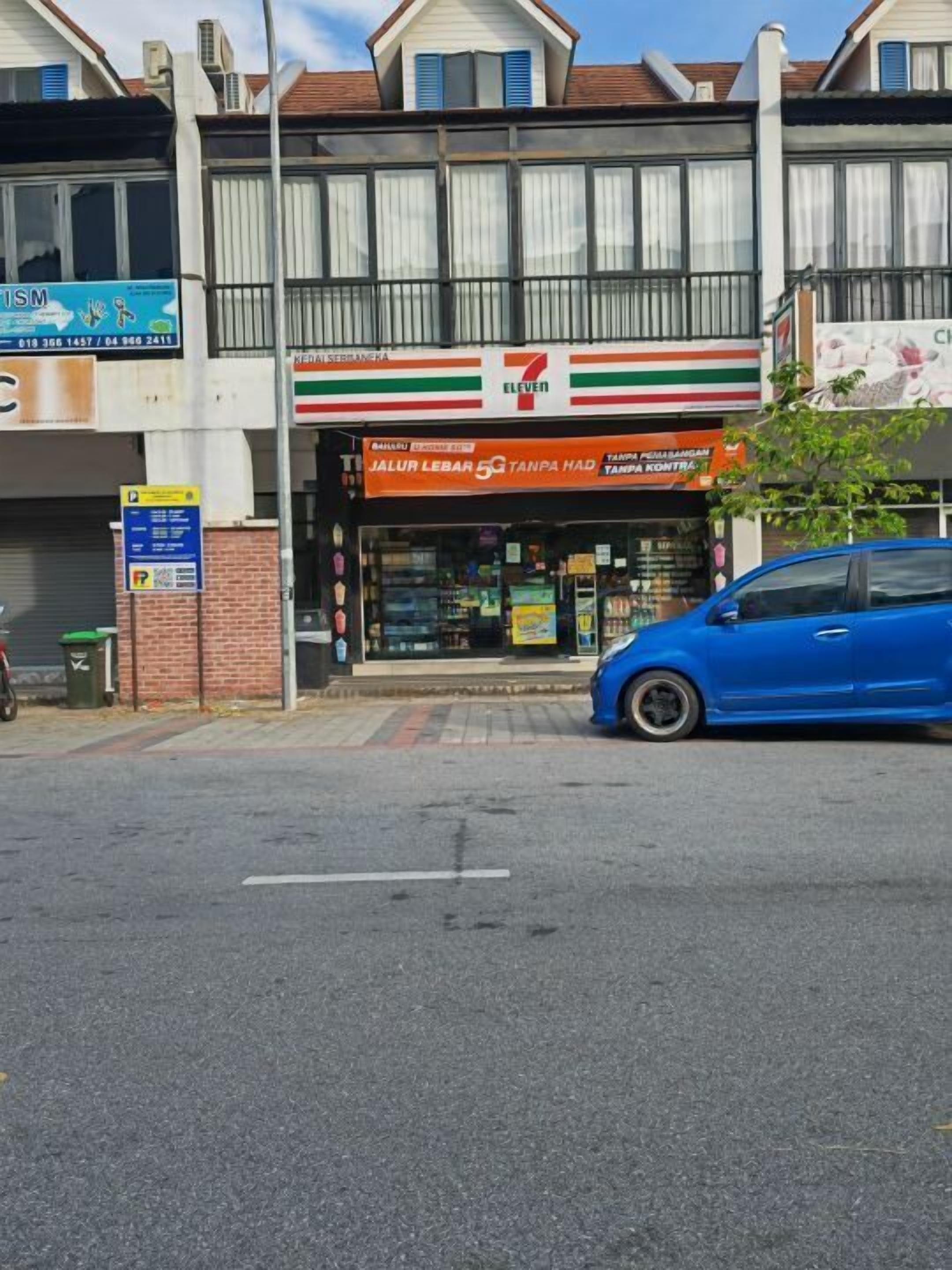 Uma loja de conveniência 7-Eleven com um sinal de 5G, um carro azul estacionado e fachada de um edifício de tijolos.