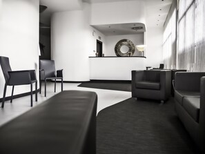 Um hall de hotel moderno com uma mesa de recepção, área de estar e um espelho grande.
