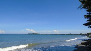 Uma praia com ondas, céu claro e uma ilha ao longe.