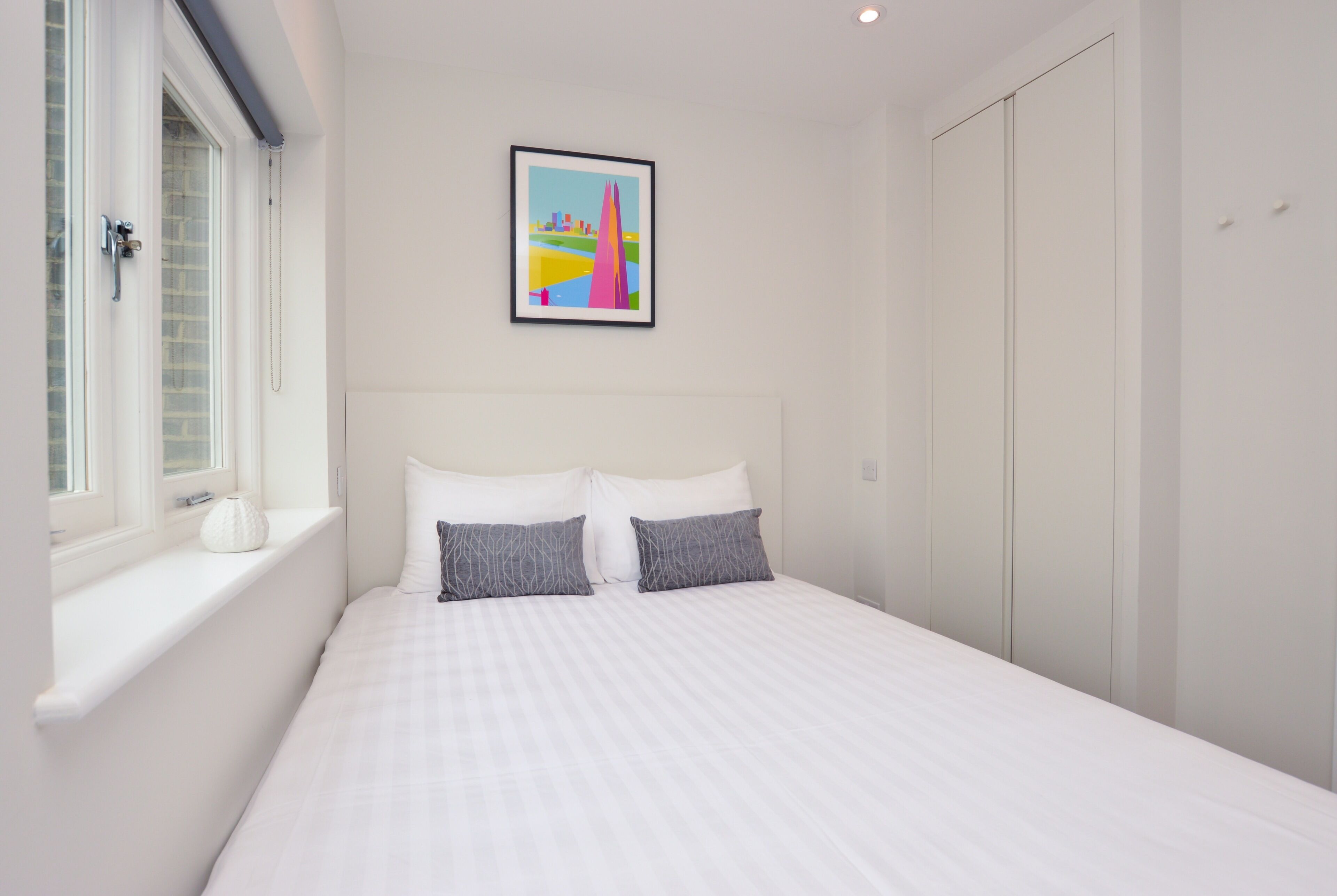 Quarto com cama, janela, quadro e guarda-roupa.
