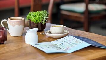 Uma mesa de madeira com um jarro branco, uma chávena de café, uma pequena planta em vaso e um menu.