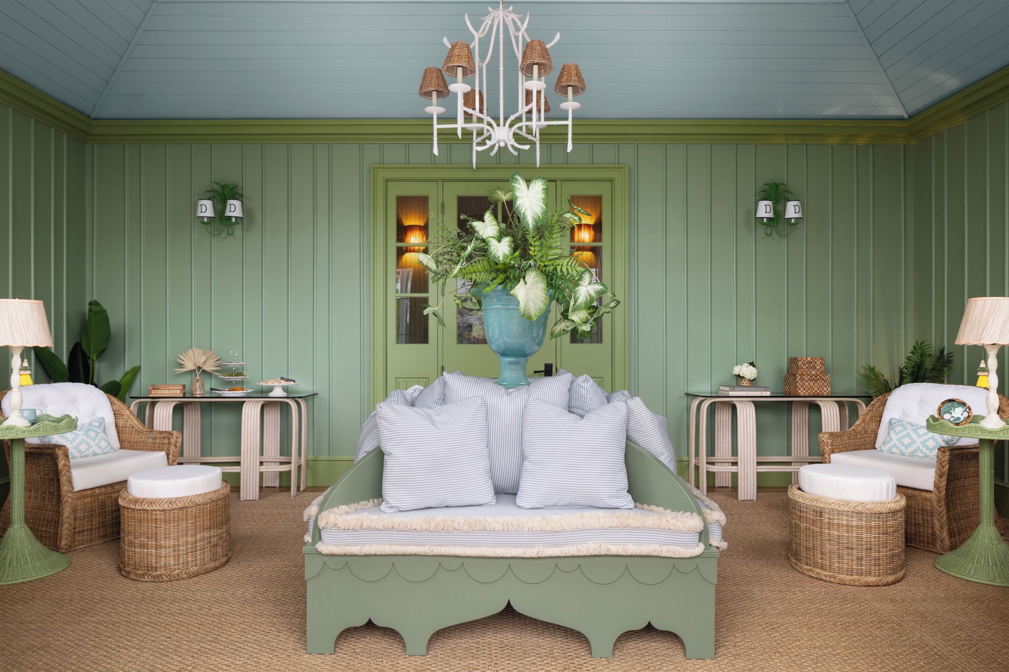 Um quarto com parede verde, cama com almofadas listradas, um lustre e duas mesas de cabeceira com abajures.