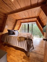 Quarto no estilo loft com teto inclinado, paredes de madeira e uma grande janela.