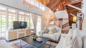 Uma sala de estar espaçosa com uma TV grande, móveis brancos e uma escada que dá para um andar superior.