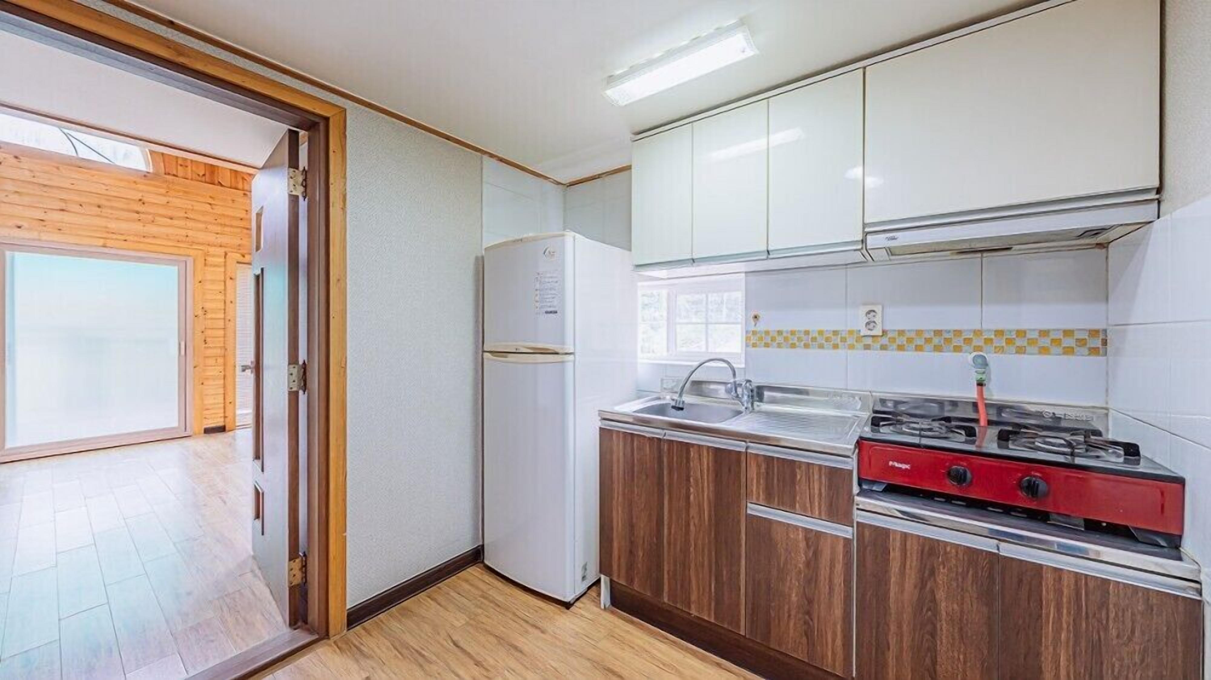 Uma cozinha compacta com armários de madeira, geladeira branca, fogão a gás e painel de azulejos.